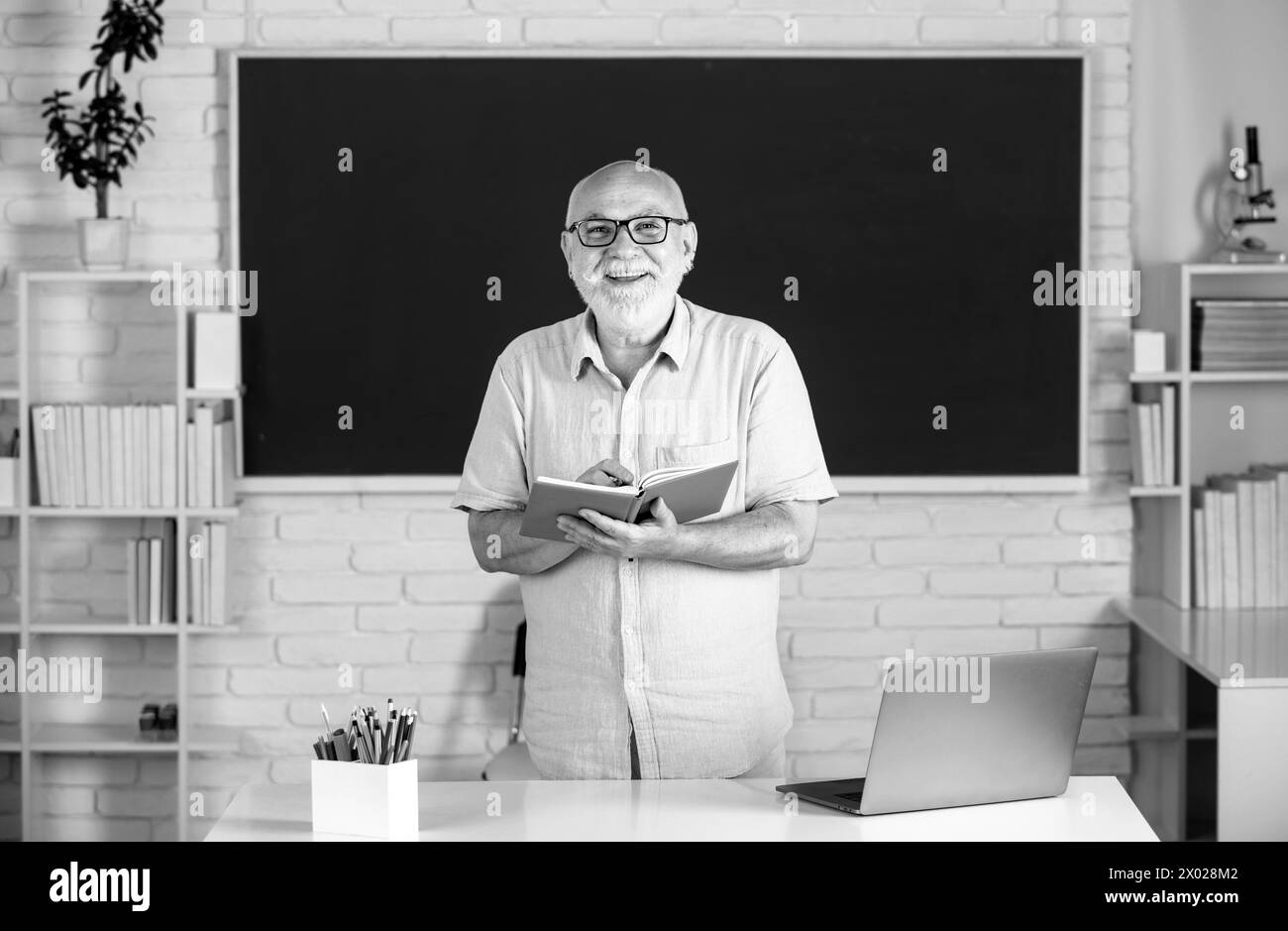 Senior teacher in the classroom on blackboard background. Old professor ...