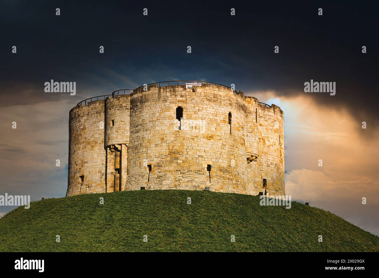 Dramatic sky over an ancient stone fortress atop a lush green hill ...