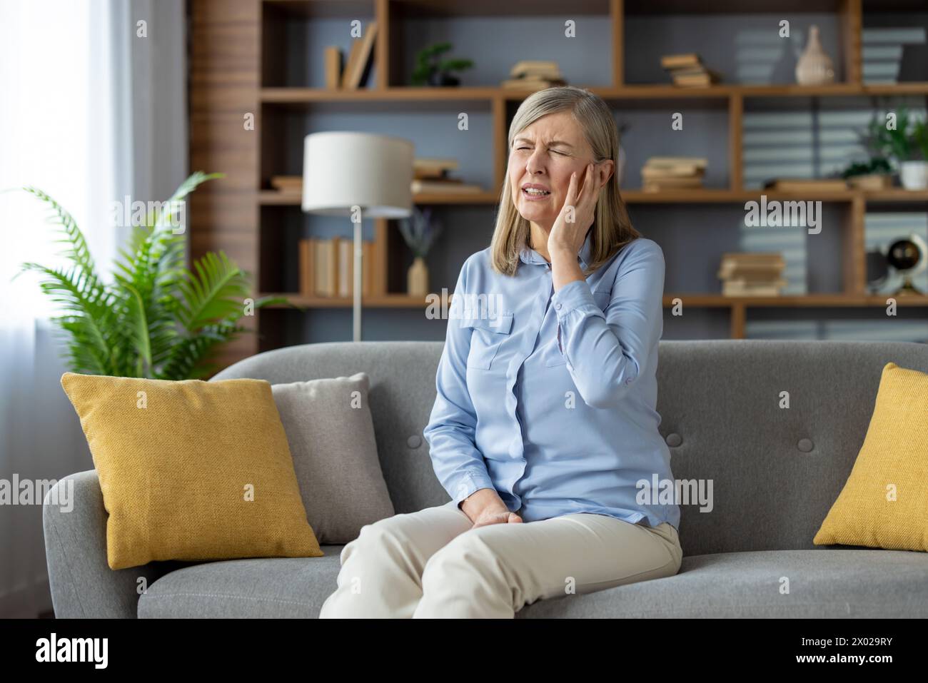Distressed person sitting on grey couch and grabbing face with palm ...