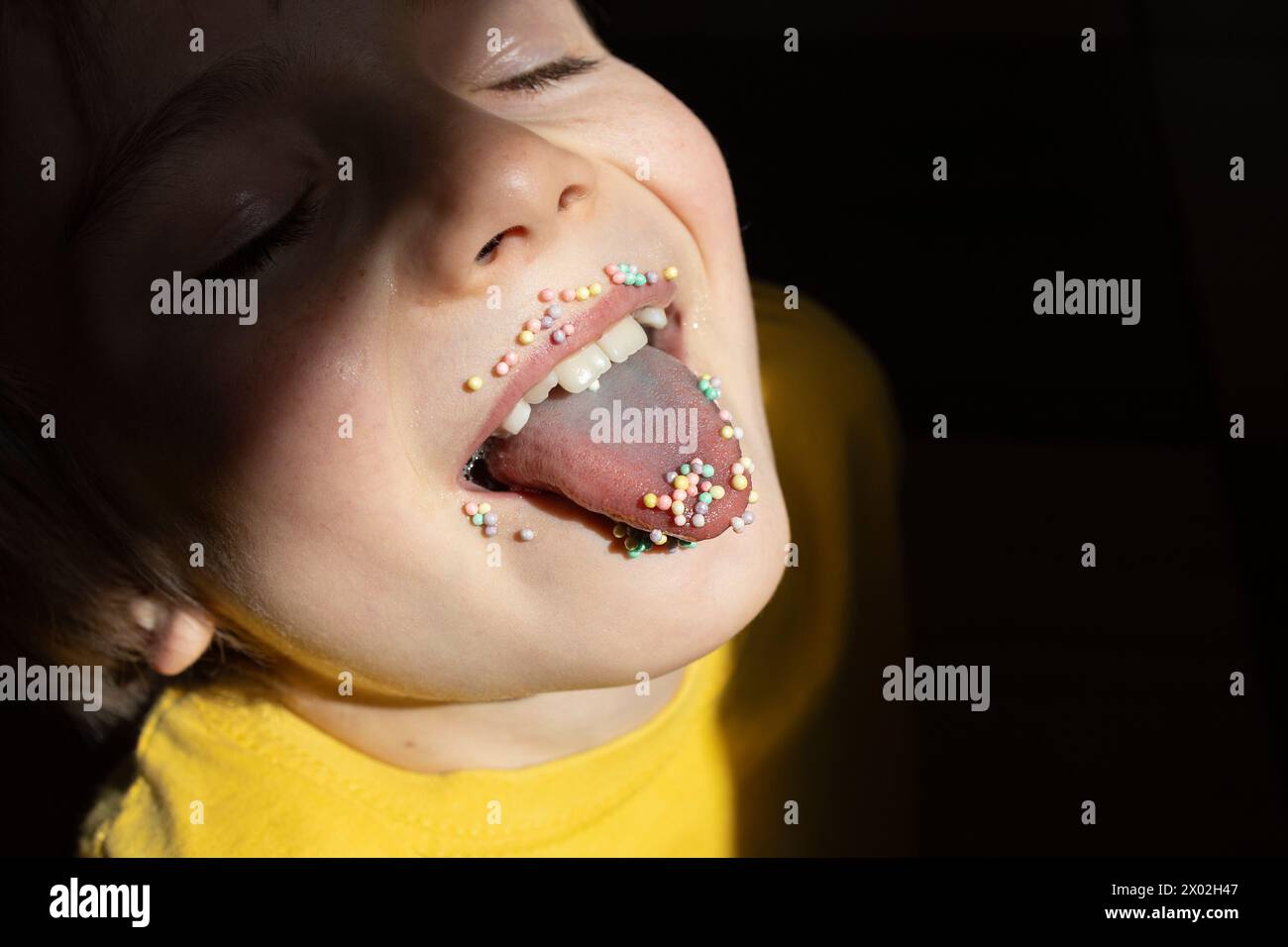 The child is having fun, licking the confectionery decorative sprinkles ...