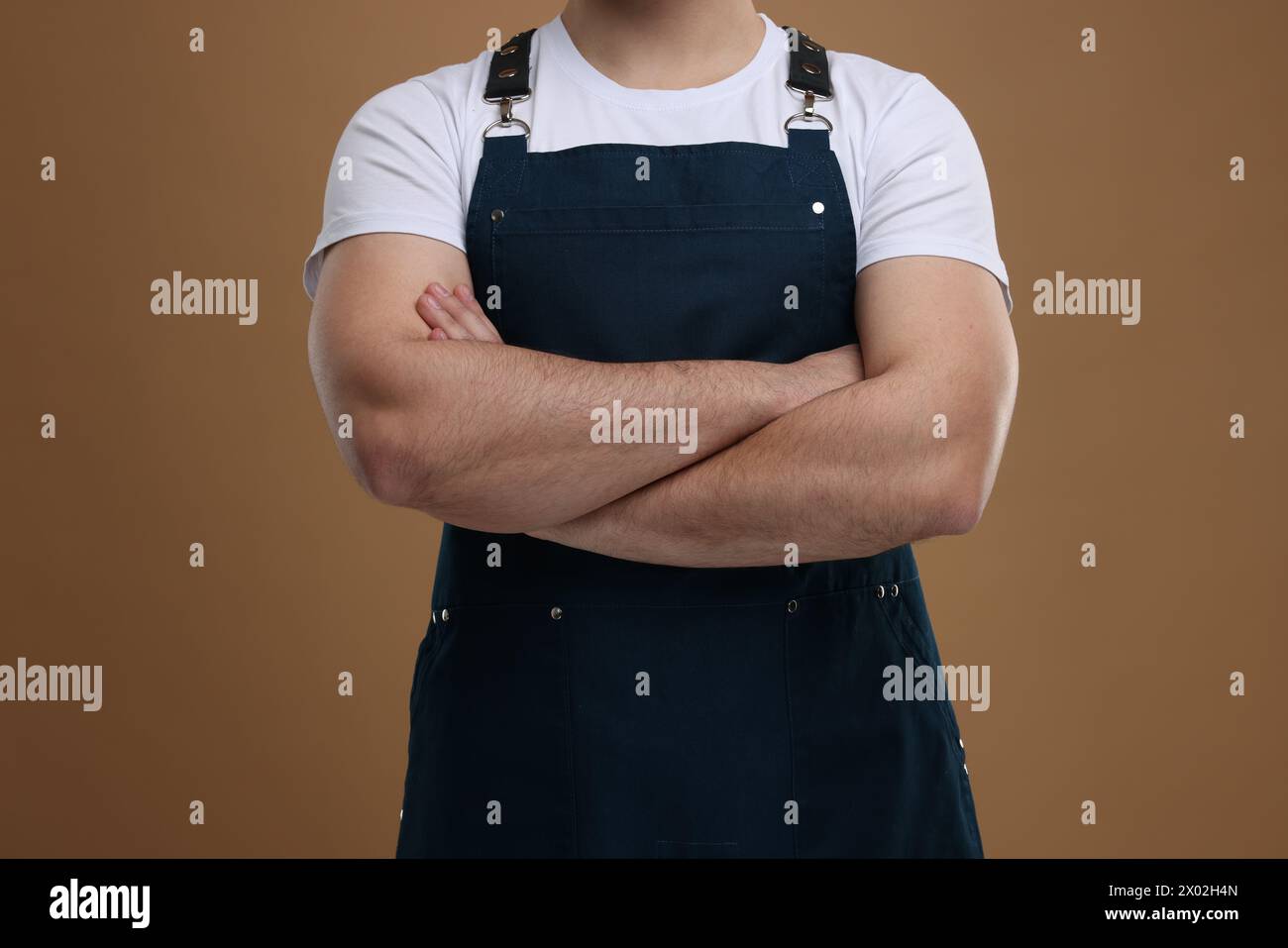 Man in kitchen apron with crossed arms on brown background, closeup ...