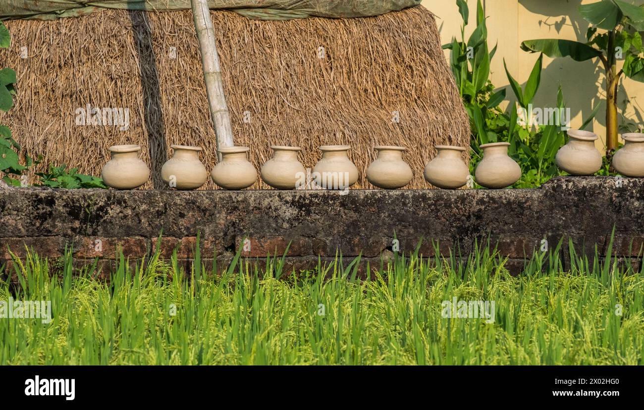 A row of recently thrown pots dries in the sun on a brick wall by a ...