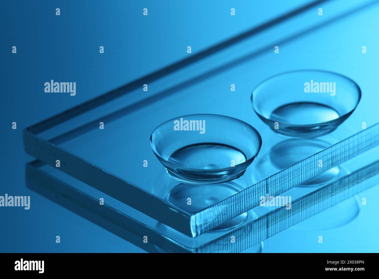 Pair of contact lenses and glass on mirror surface, closeup. Toned in ...