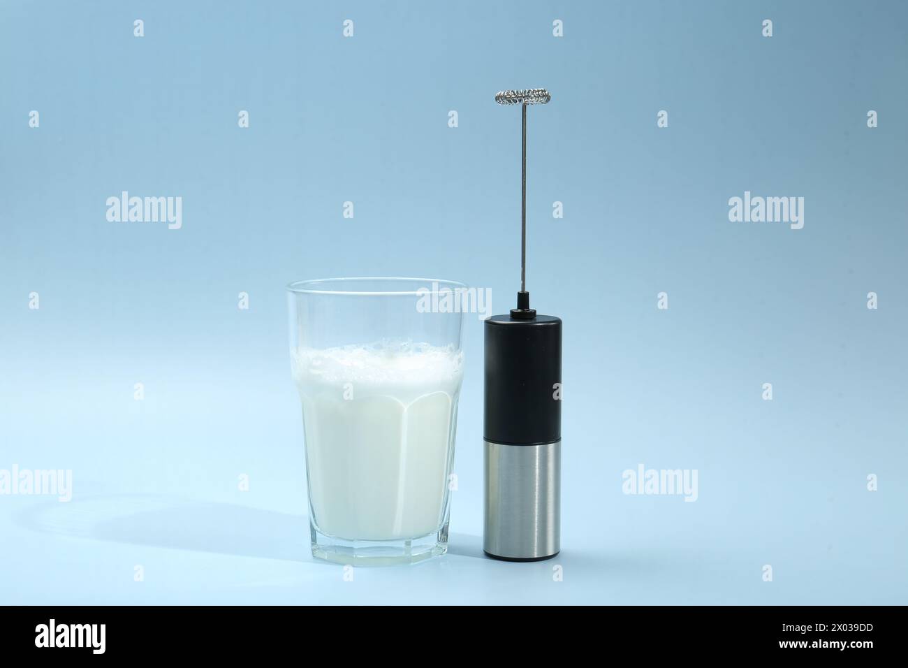 Mini mixer (milk frother) and whipped milk in glass on light blue ...