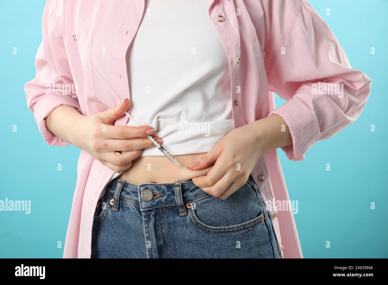 Diabetes. Woman making insulin injection into her belly on light blue ...