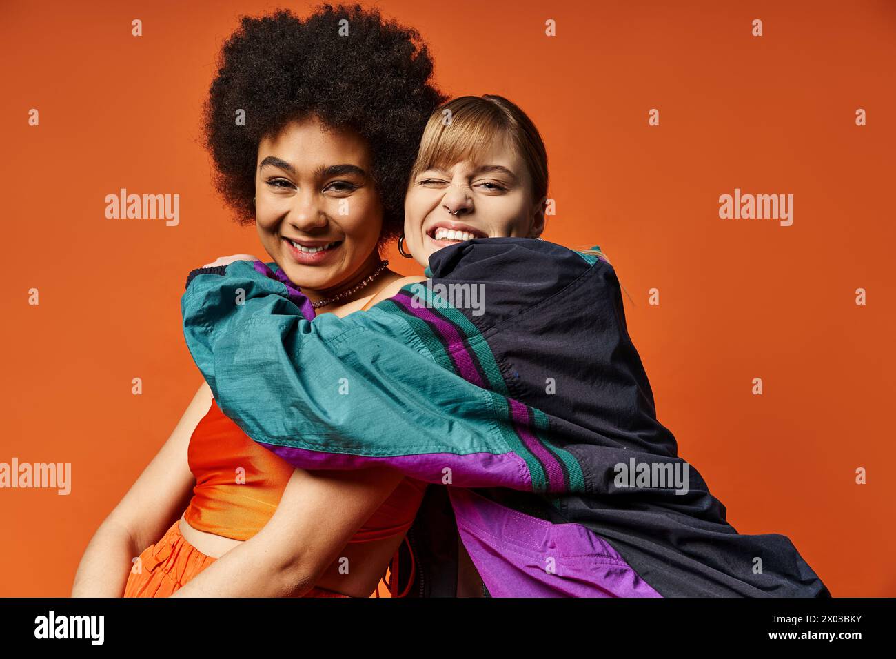 Two women of different races standing together against an orange ...