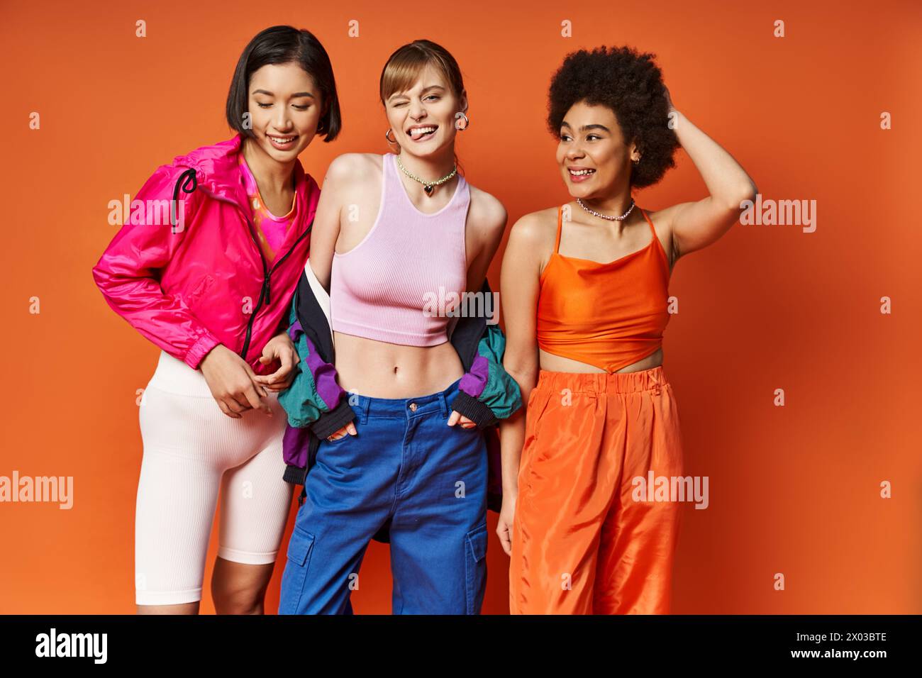 Three diverse women standing side by side against an orange studio ...