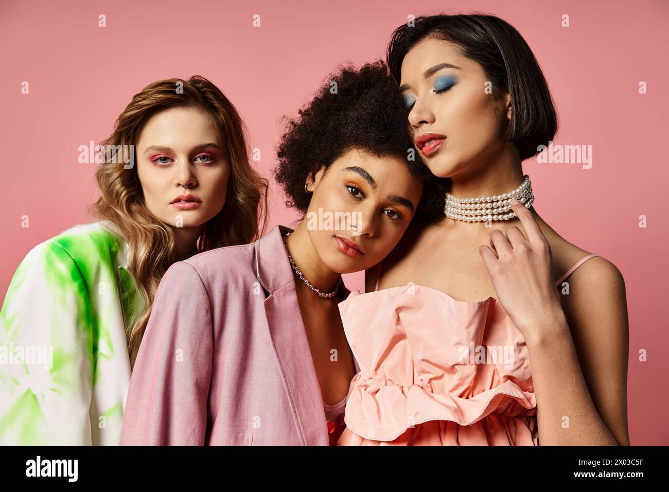 Three women of different ethnicities standing together on a pink studio ...