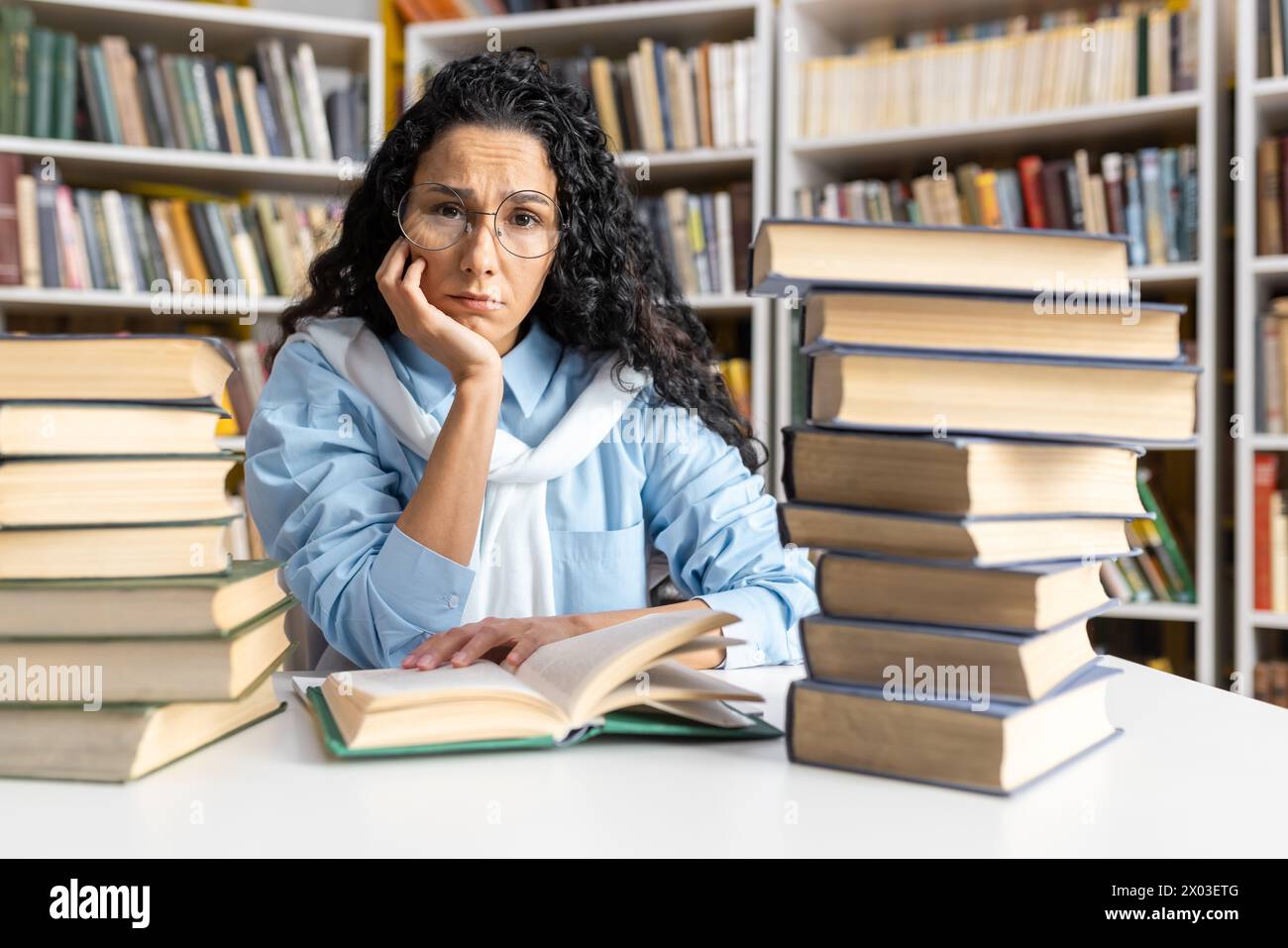 Worried hispanic female student studying hard in a library. She is ...