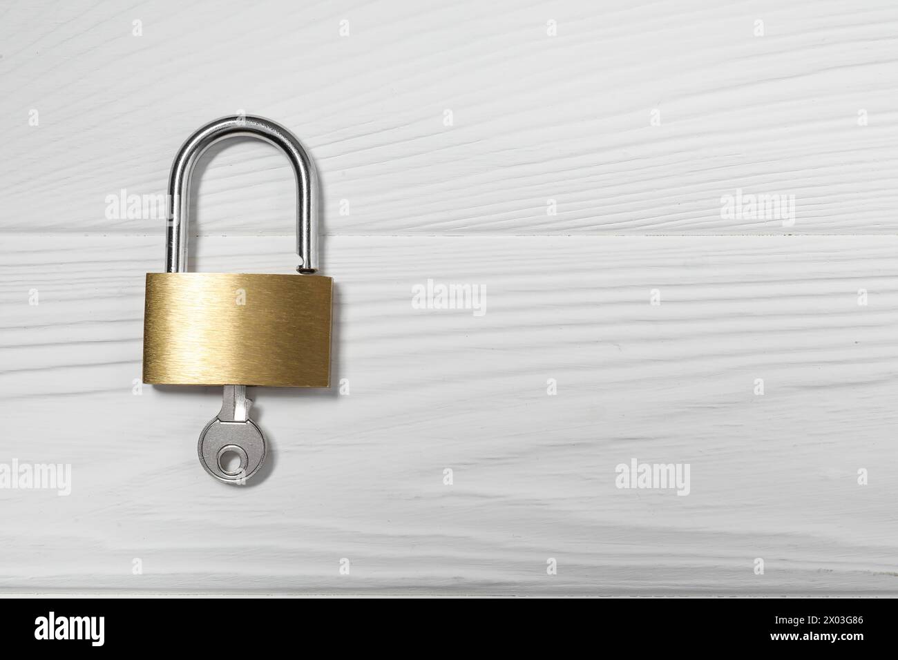 Steel padlock with key on white wooden table, top view. Space for text ...