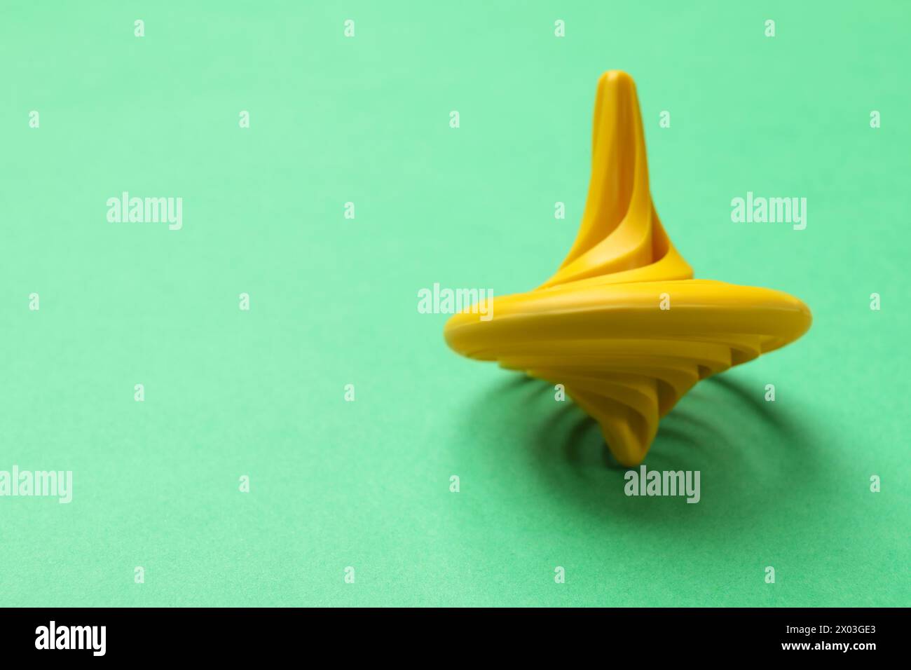 One yellow spinning top on green background, closeup. Space for text ...