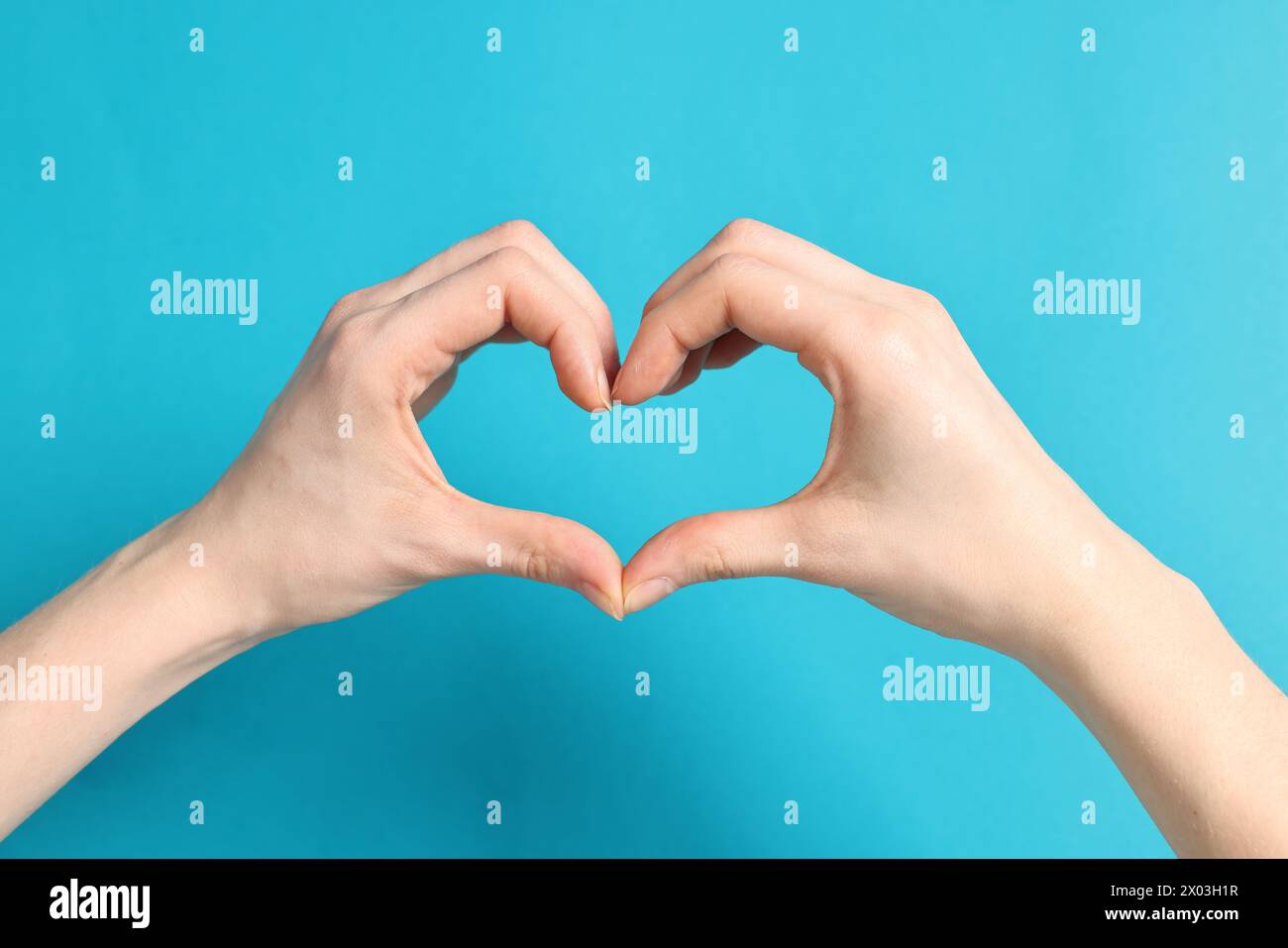 Woman showing heart gesture with hands on light blue background ...