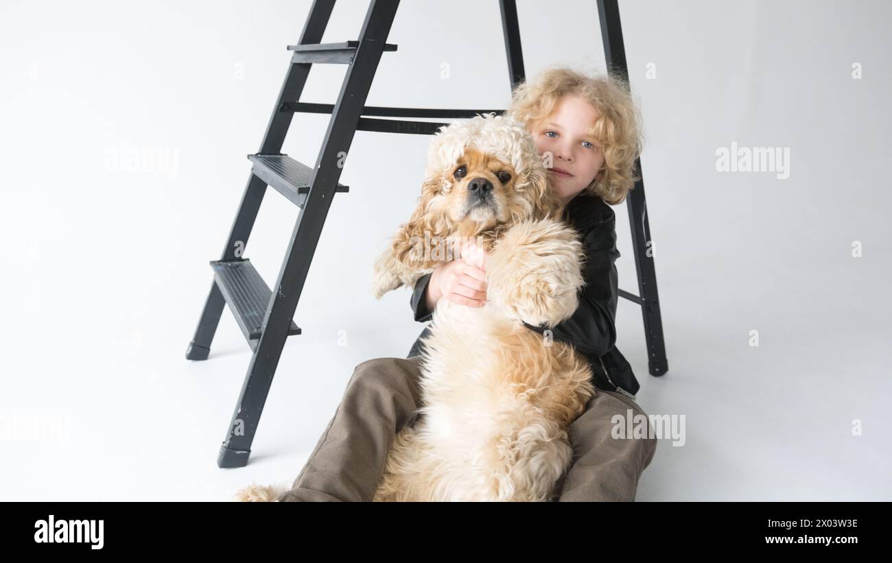 A young boy with curly blond hair is sitting on the floor leaning ...