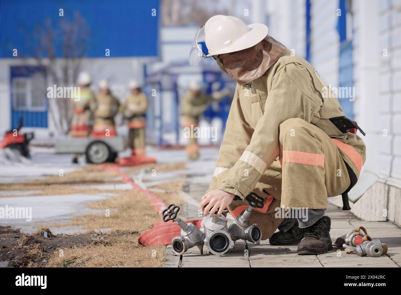 A firefighter is crouched down attaching a hose to a fire hydrant, with ...