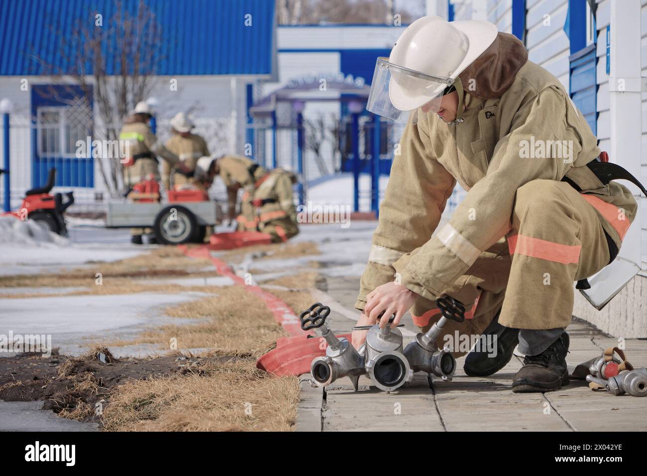 A firefighter is crouched down attaching a hose to a fire hydrant, with ...