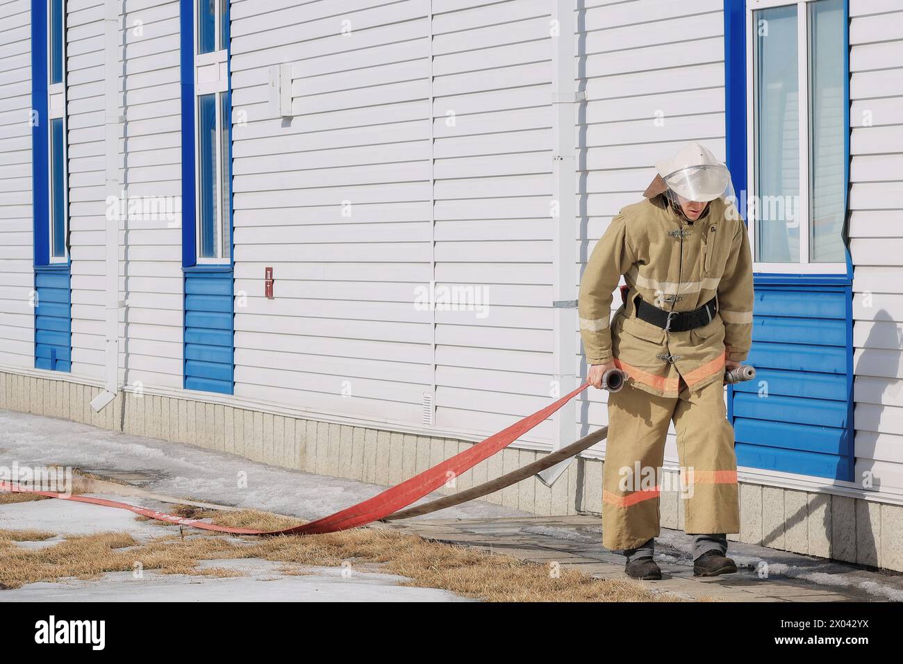 An image of a firefighter in uniform rolling a red hose after use, with ...