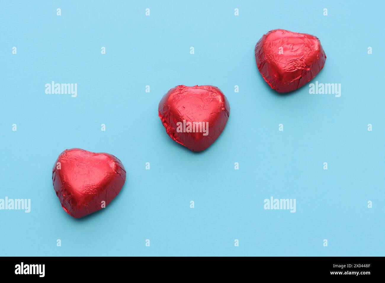 Three heart-shaped chocolates wrapped in red foil, top view Stock Photo ...