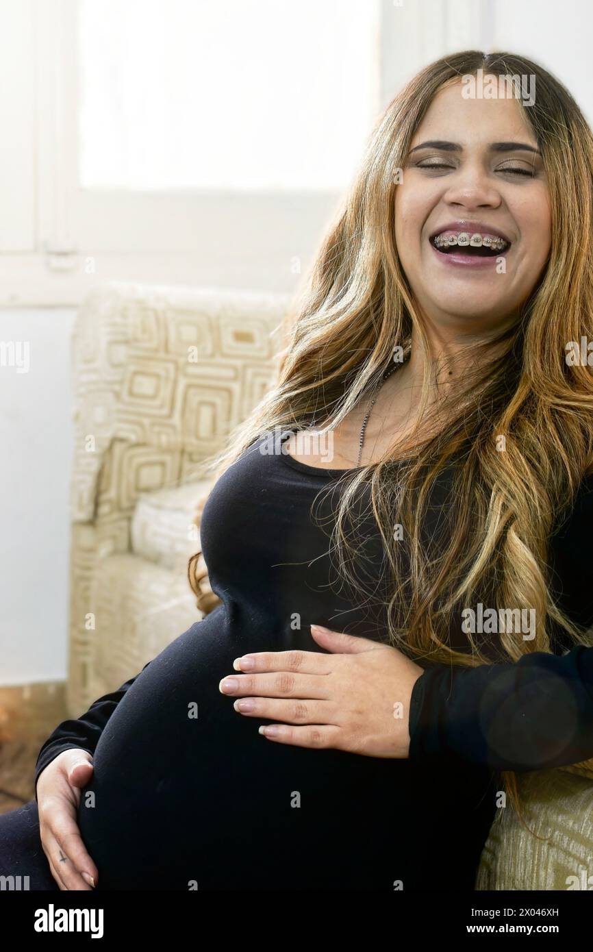 Pregnant Woman Smiling At Camera While One Of Her Hands Touches Her