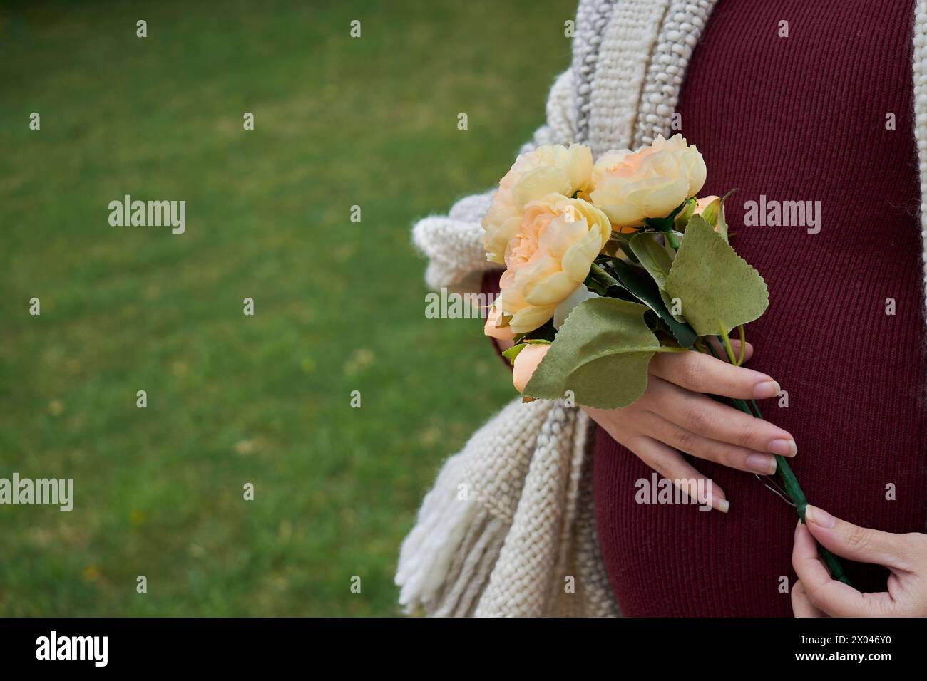 Pregnant woman's belly with a bouquet of flowers in her hand. She has a ...