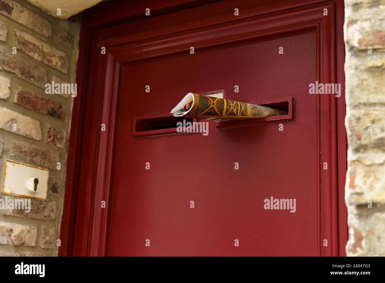 A newspaper is halfway through a mail slot in a red door framed by ...