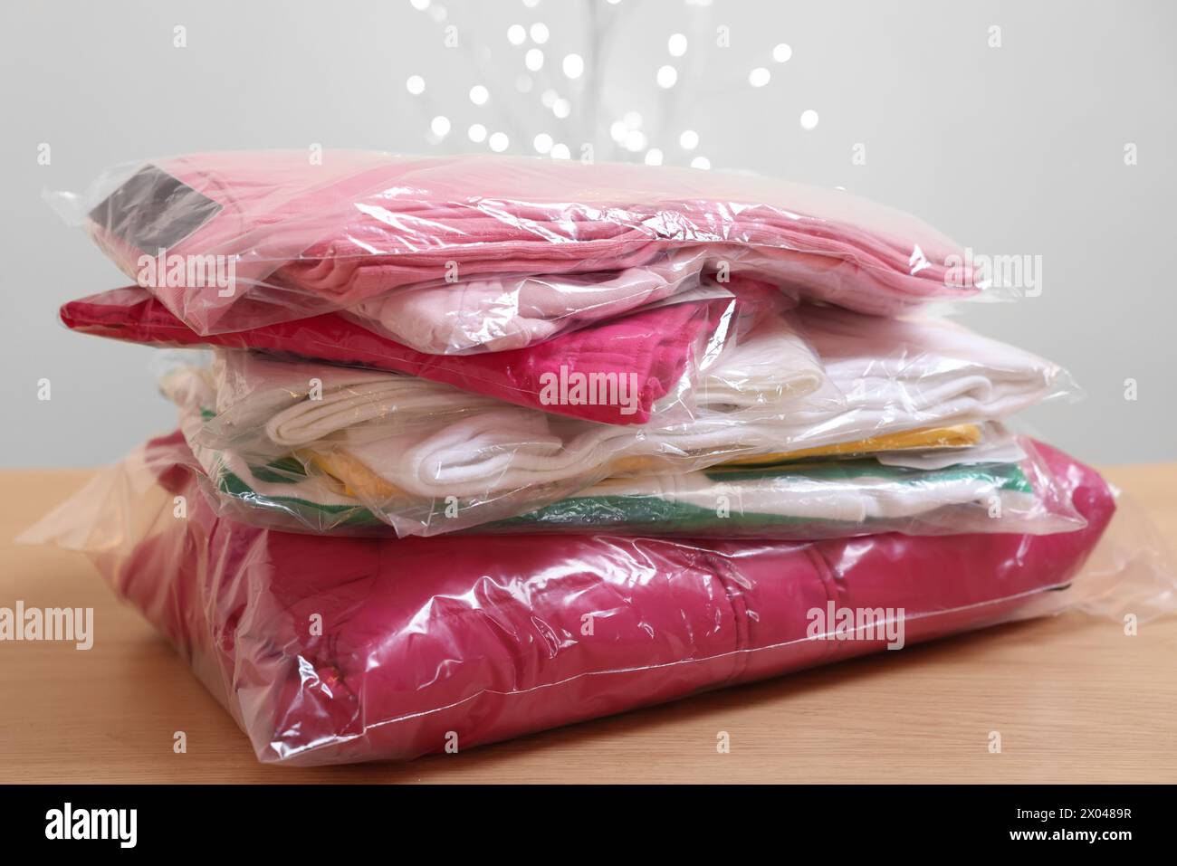 Stack of folded clothes in plastic bags on wooden table against beige ...