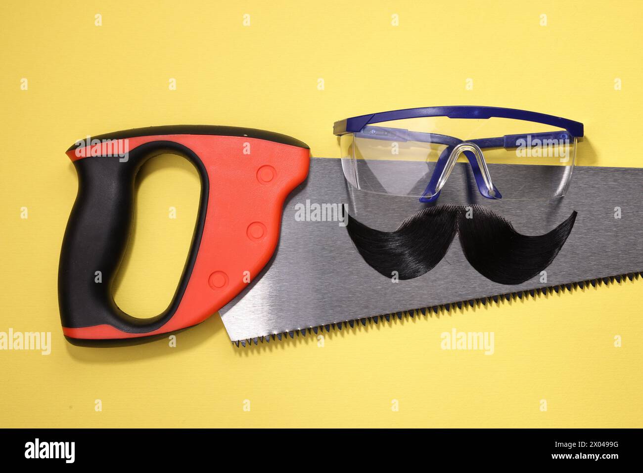 Man's face made of artificial mustache, safety glasses and hand saw on ...