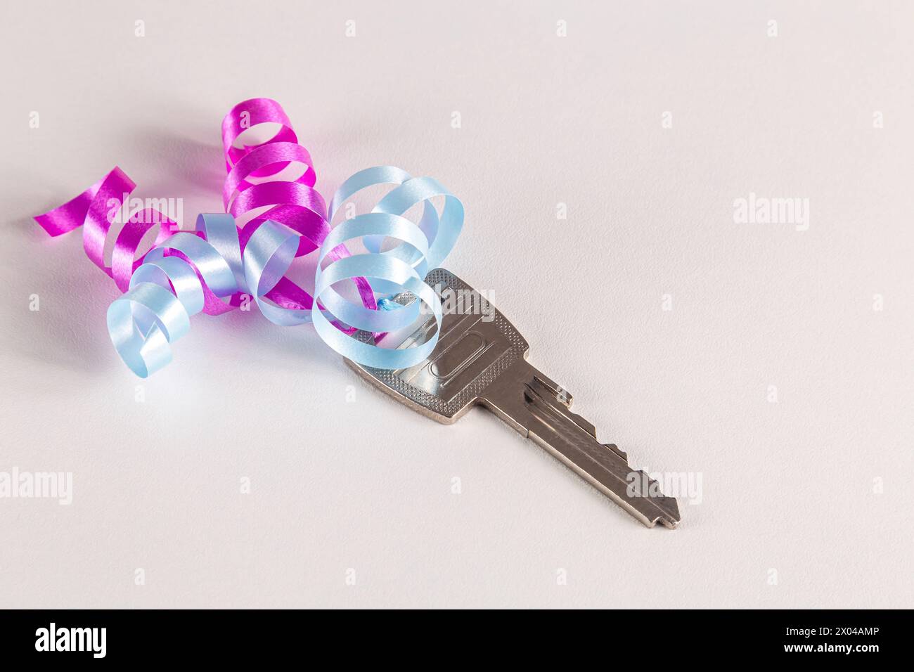 Key with pink and blue ribbon on a white surface. Place for text. Cloce ...