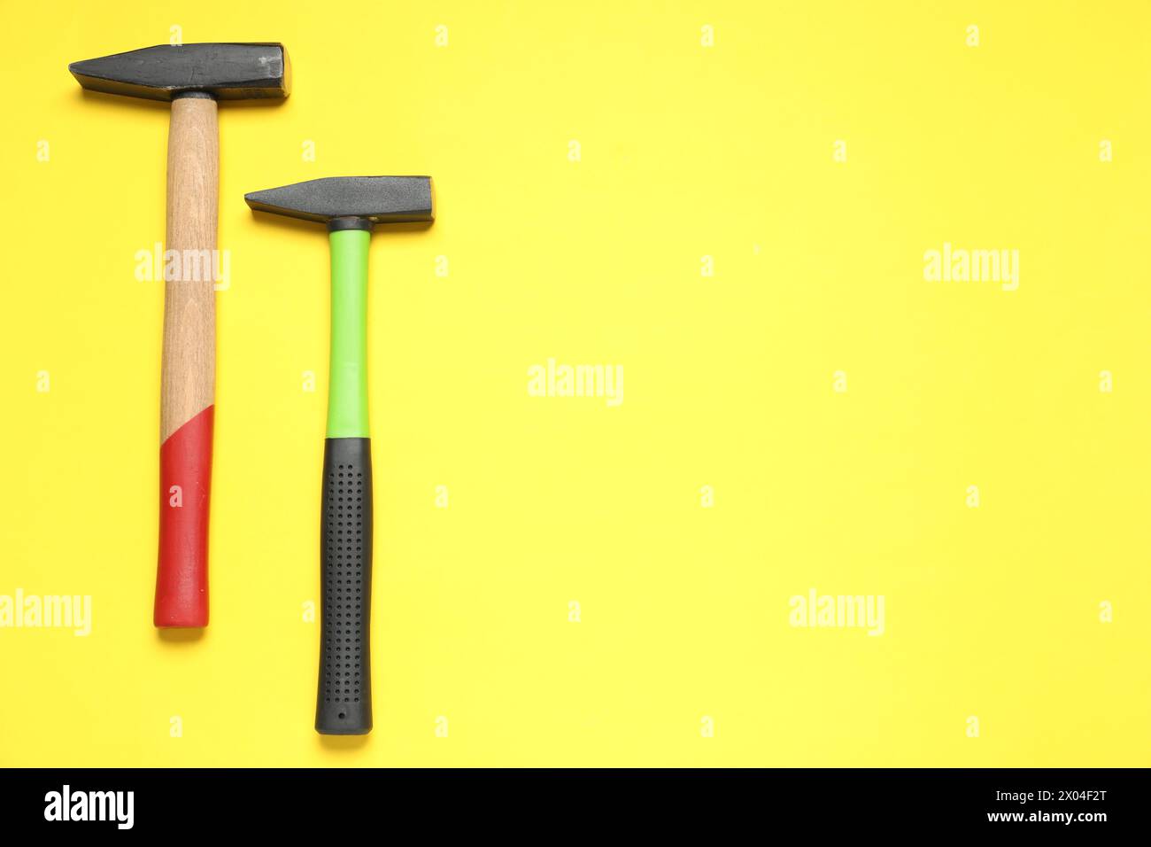Two hammers with rubber handles on yellow background, top view. Space ...