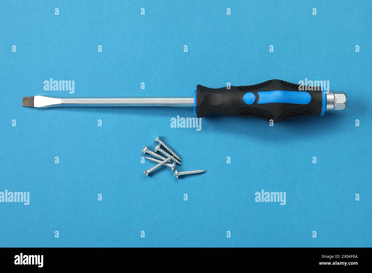 Screwdriver with black handle and screws on blue background, flat lay ...