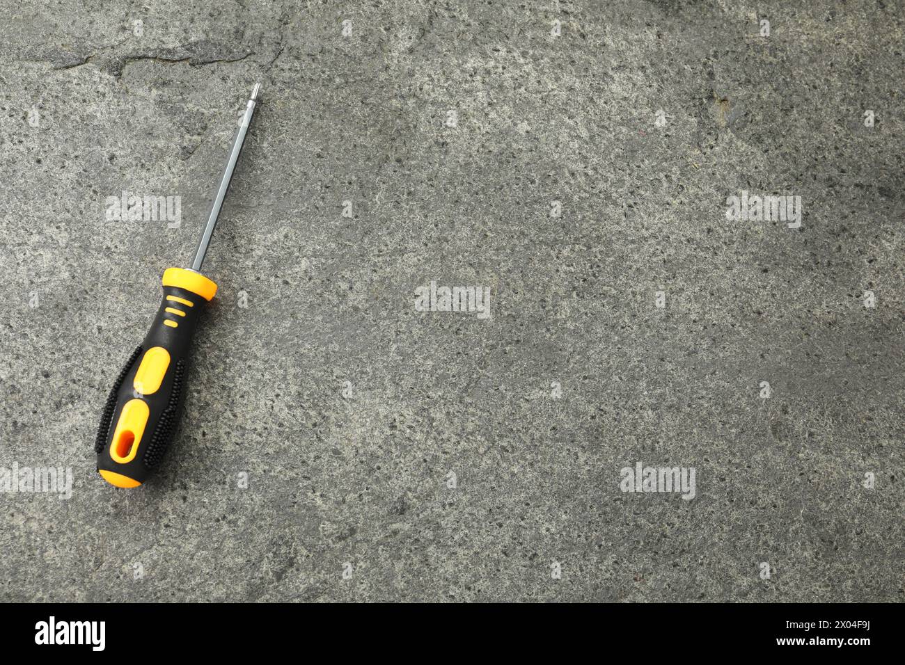Screwdriver with black handle on grey textured table, top view. Space ...