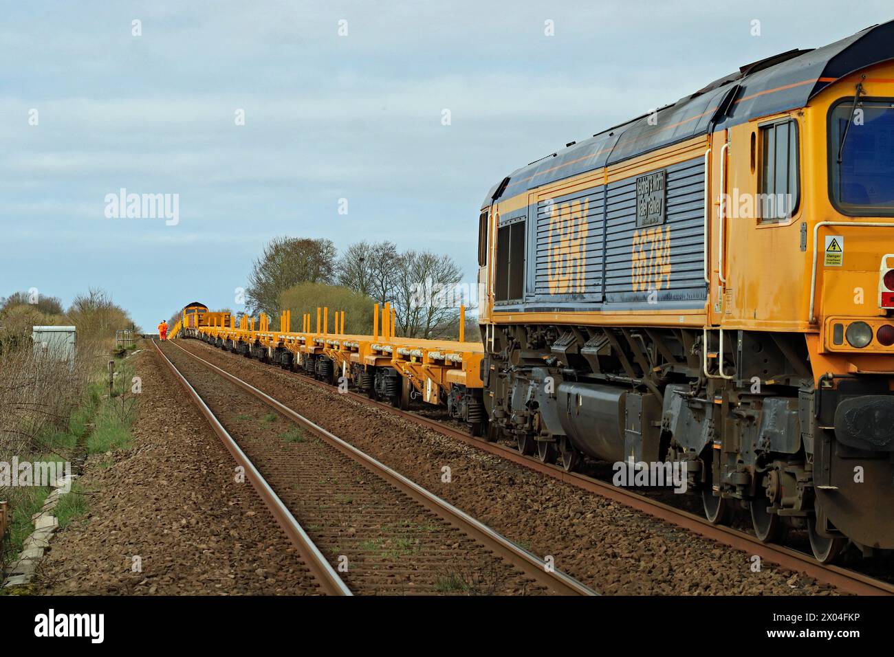 A long line of engineering trains stand along a hilly section of track ...