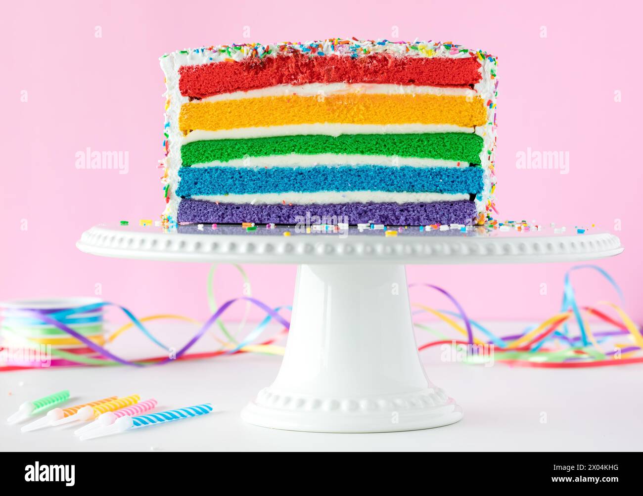 A rainbow cake with sprinkles, candles and colourful ribbons Stock ...