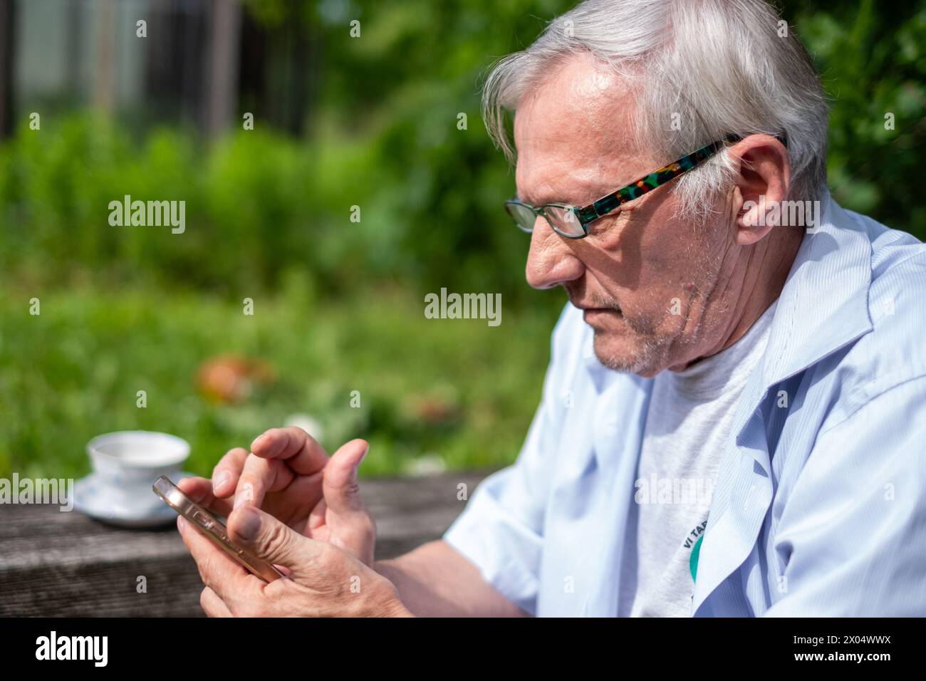 Gray haired man in spectacles interacts with his mobile device, seated ...