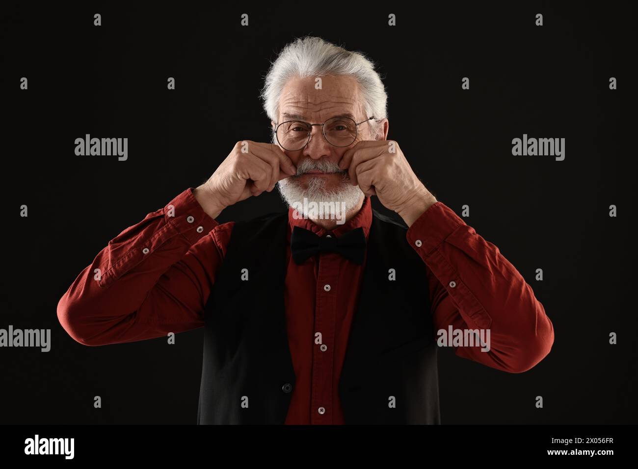 Senior man touching mustache on black background Stock Photo - Alamy
