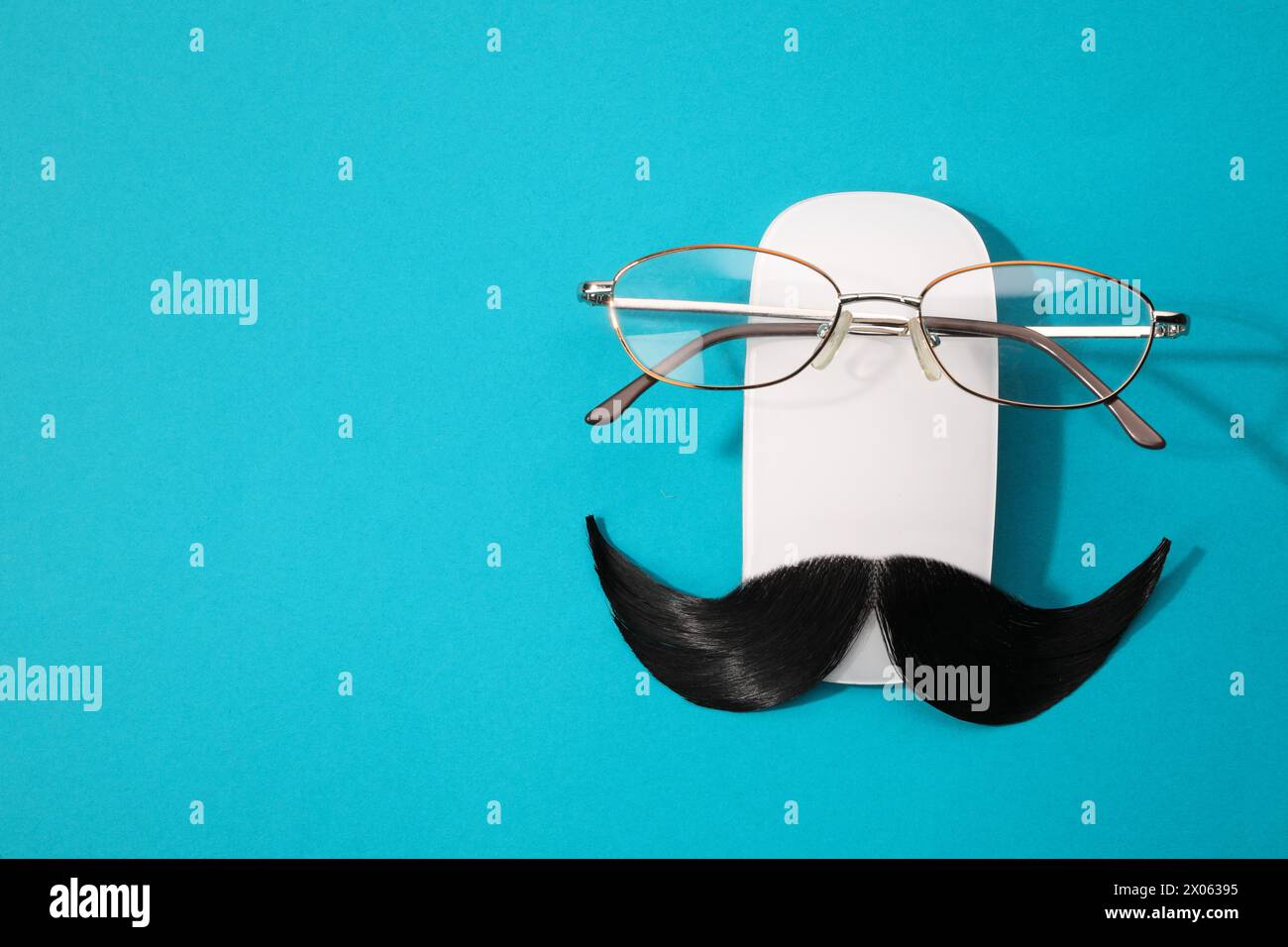 Artificial moustache, computer mouse and glasses on light blue ...