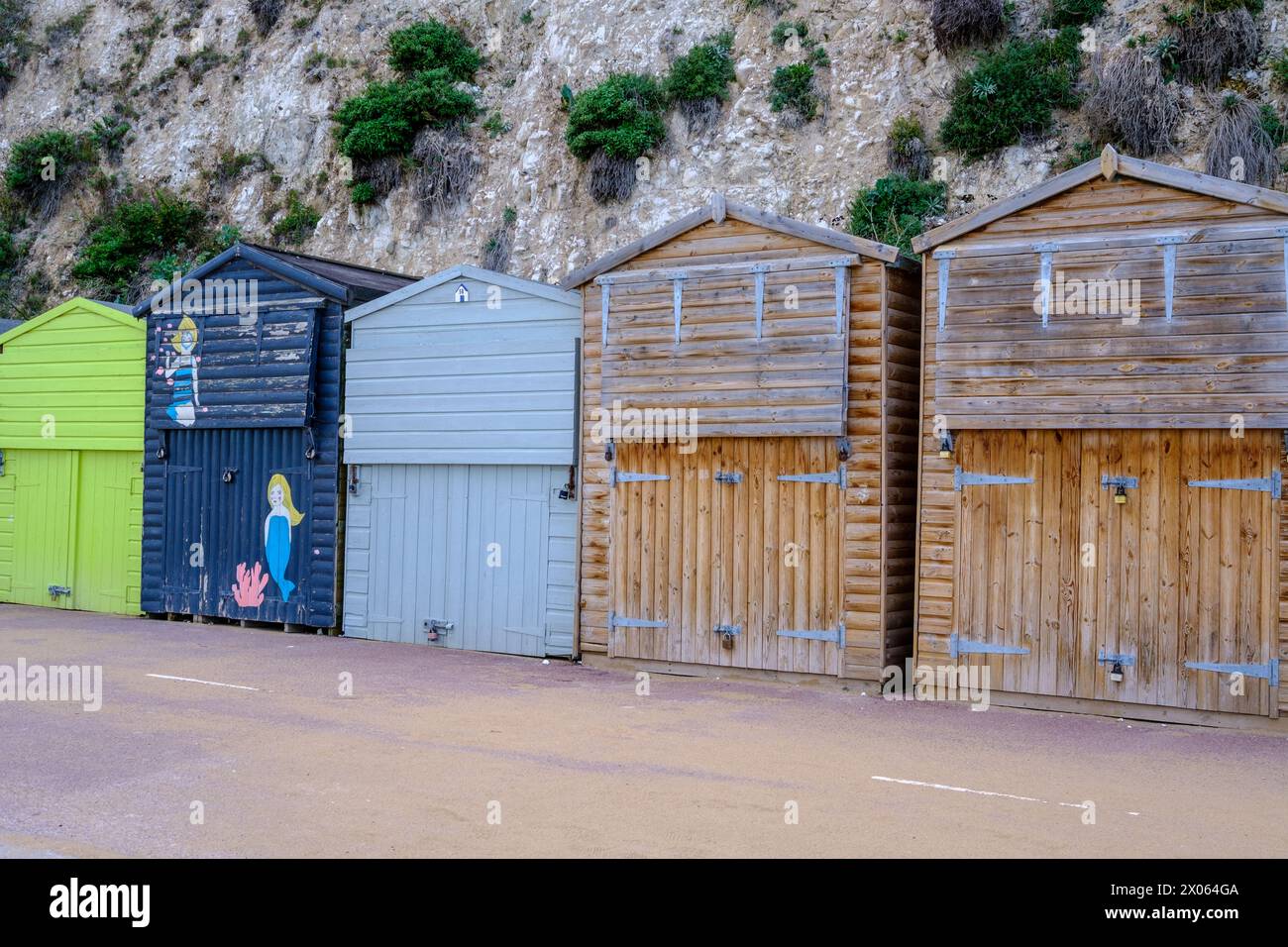 Close-up of row of vibrant, colourful beach huts at base of tall white ...