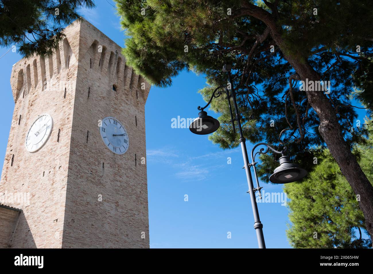 An ancient stone clock tower against a blue sky. Pine trees and a ...
