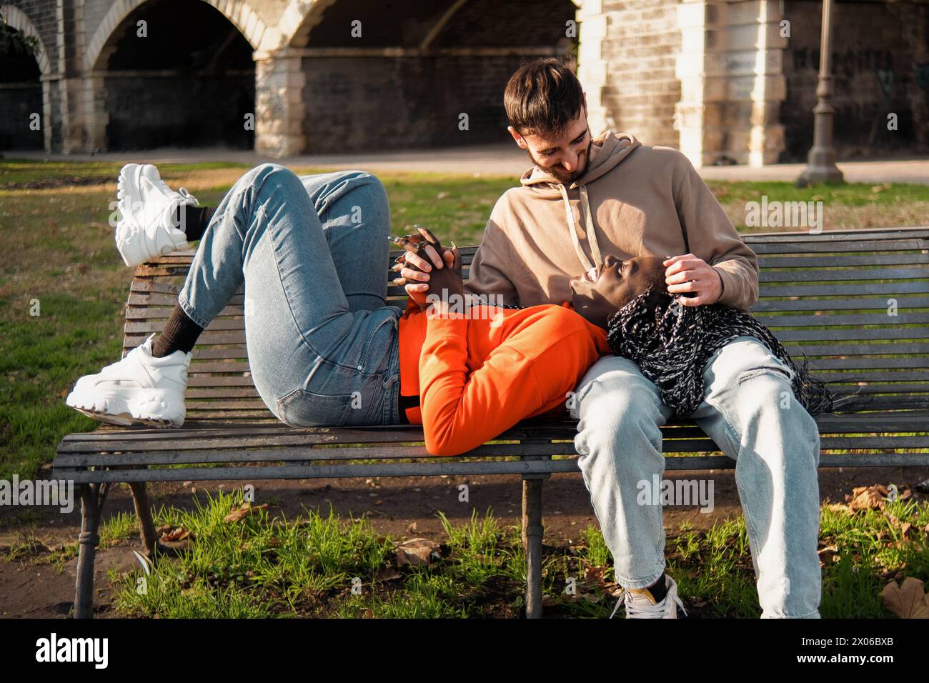 Multiethnic couple shares a tender exchange, lounging on a park bench ...
