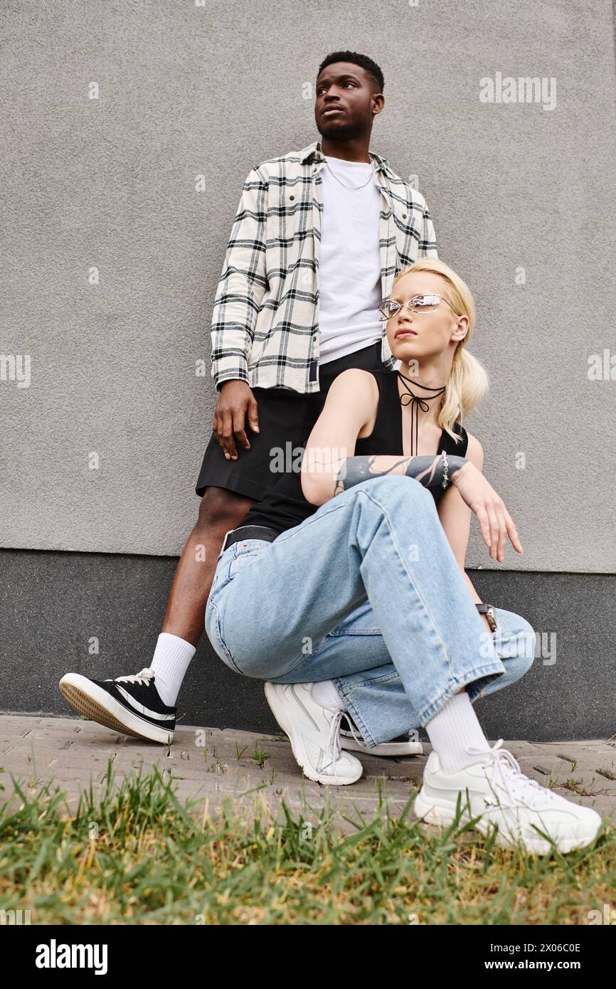 A multicultural couple happily sits together on the ground near a grey ...