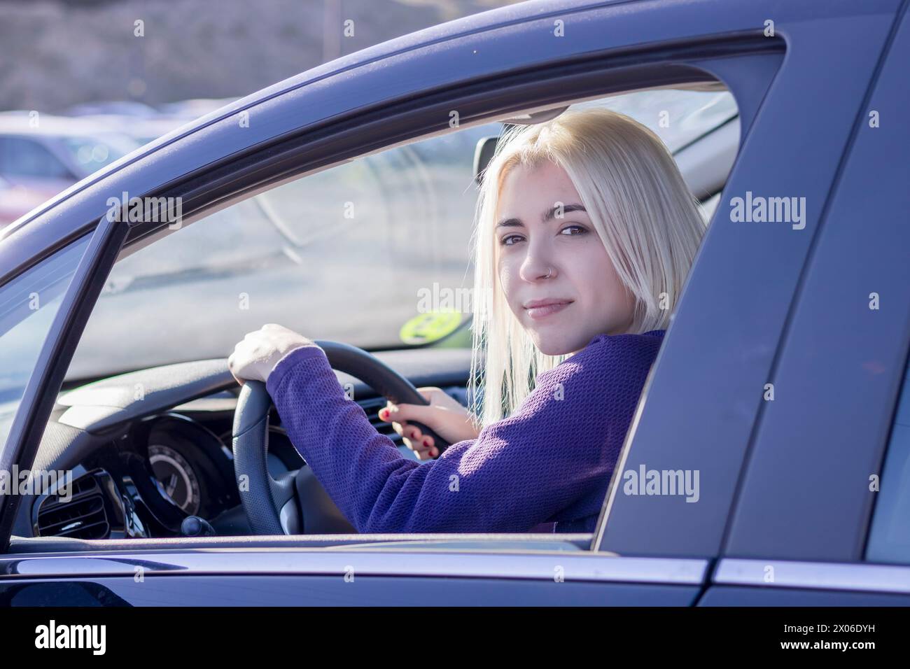 A young blonde female driver wearing a purple sweater, sitting ...