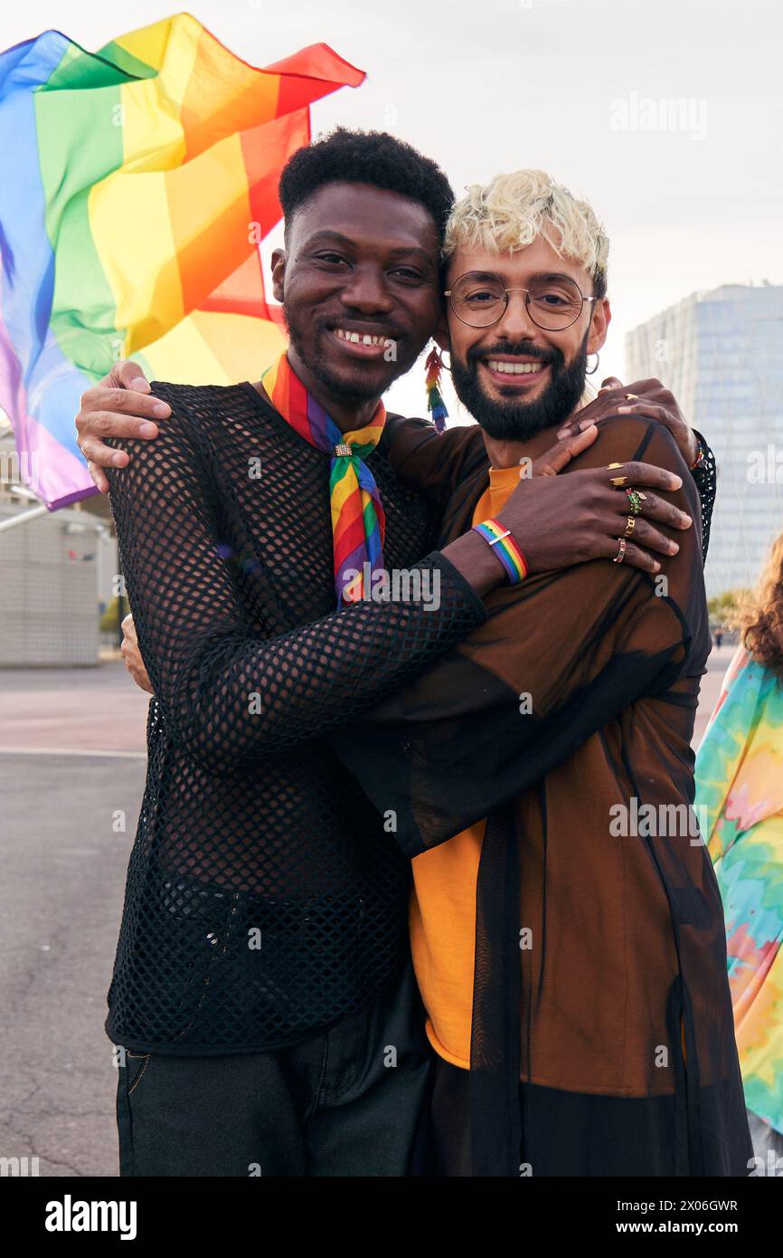 Cheerful portrait of gay couple hugging while looking at camera smiling ...
