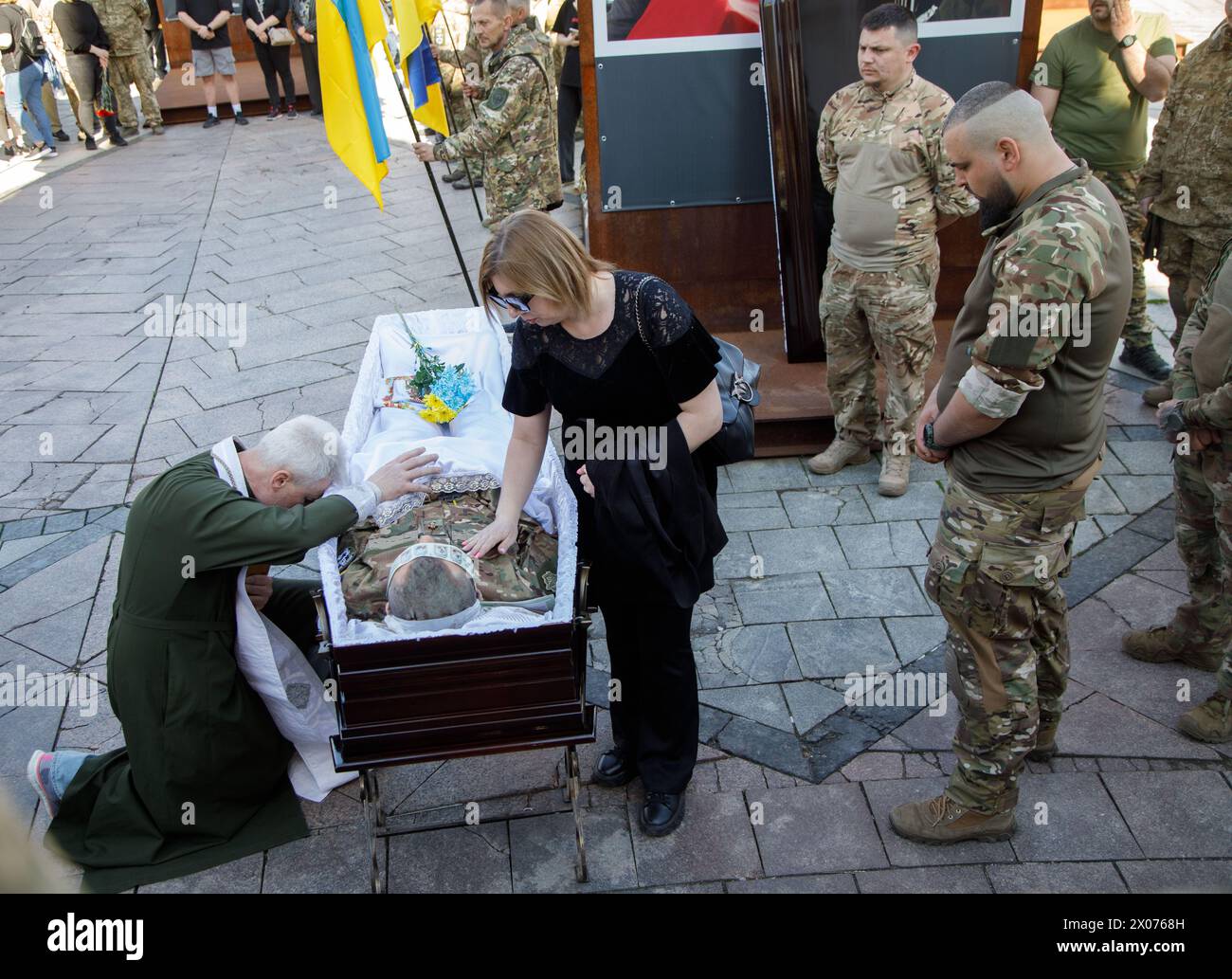 KYIV, UKRAINE - APRIL 9, 2024 - A priest kneels at a coffin during the ...