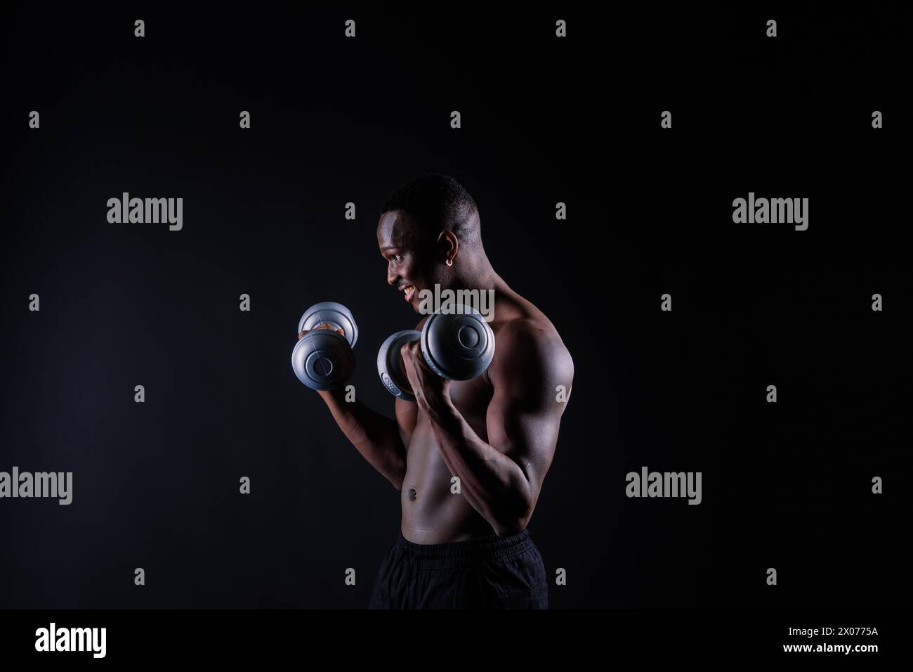 Young man with dumbbells good physique isolated on red and black ...