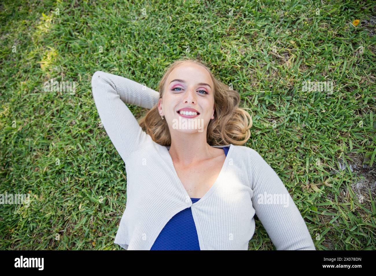 A smiling young woman is laying on the grass with her arms spread out ...