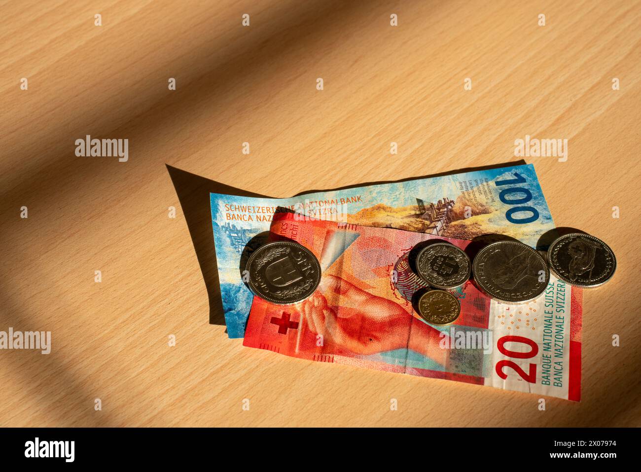 Money, bills and coins, lying on a sunlit wooden table with shadow ...