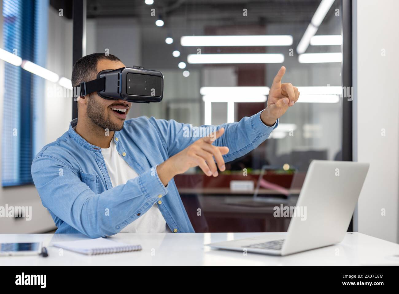 Smiling Indian man wearing virtual reality headset, interacting with digital content in a modern ...
