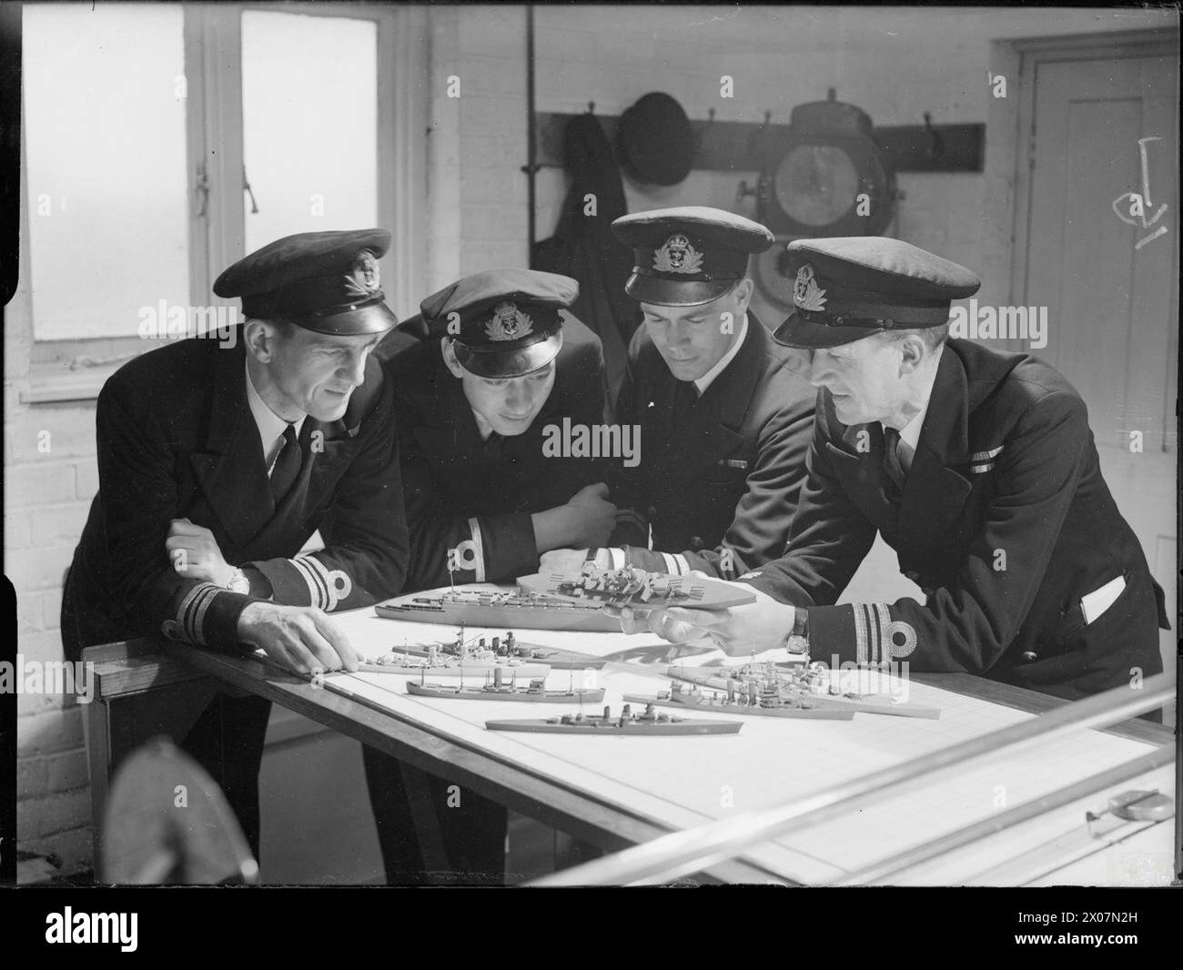 Royal Navy officers examine models of enemy ships on a plotting table ...