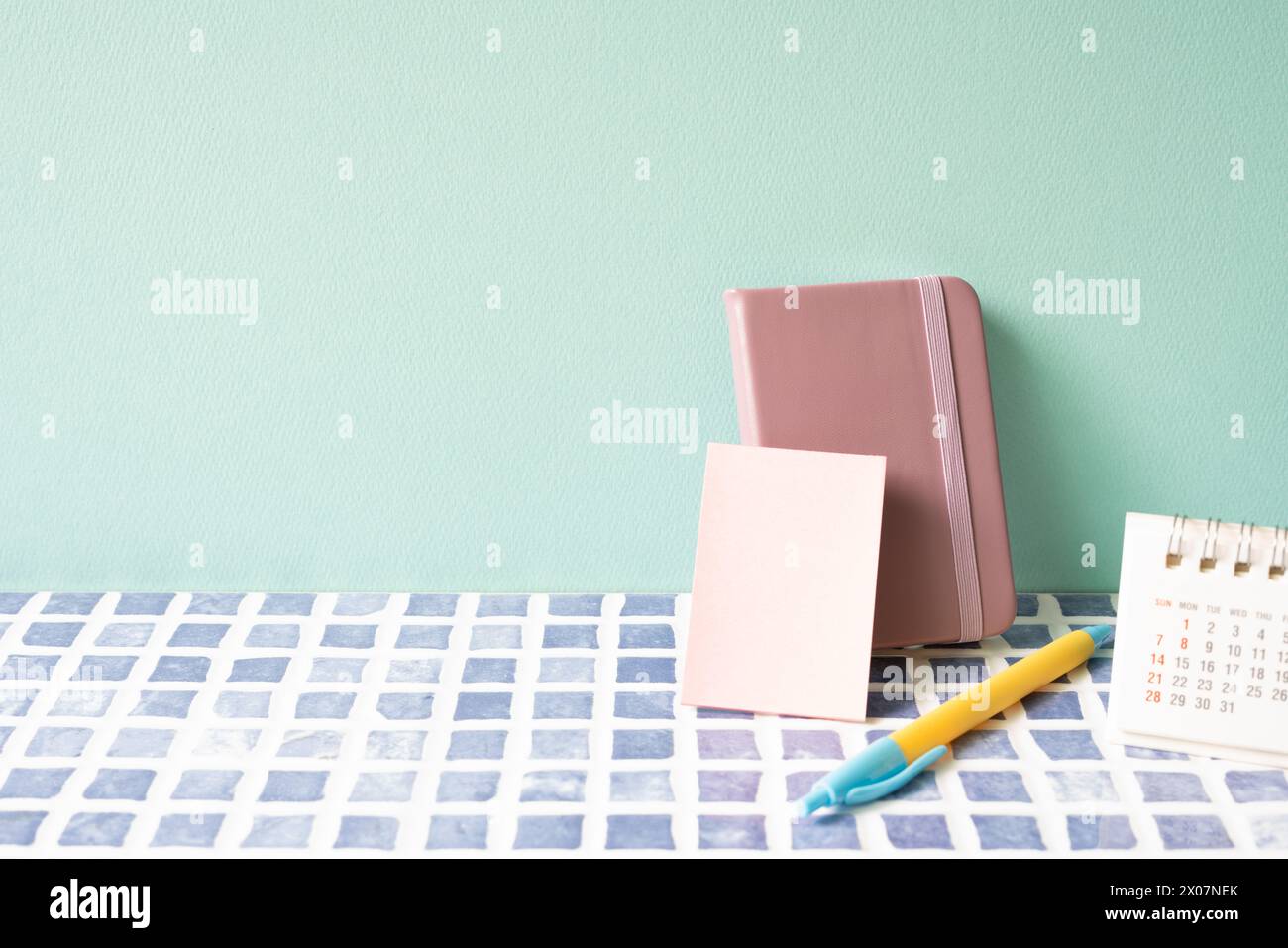 Diary note, pen, and calendar on blue tile desk. mint wall background ...