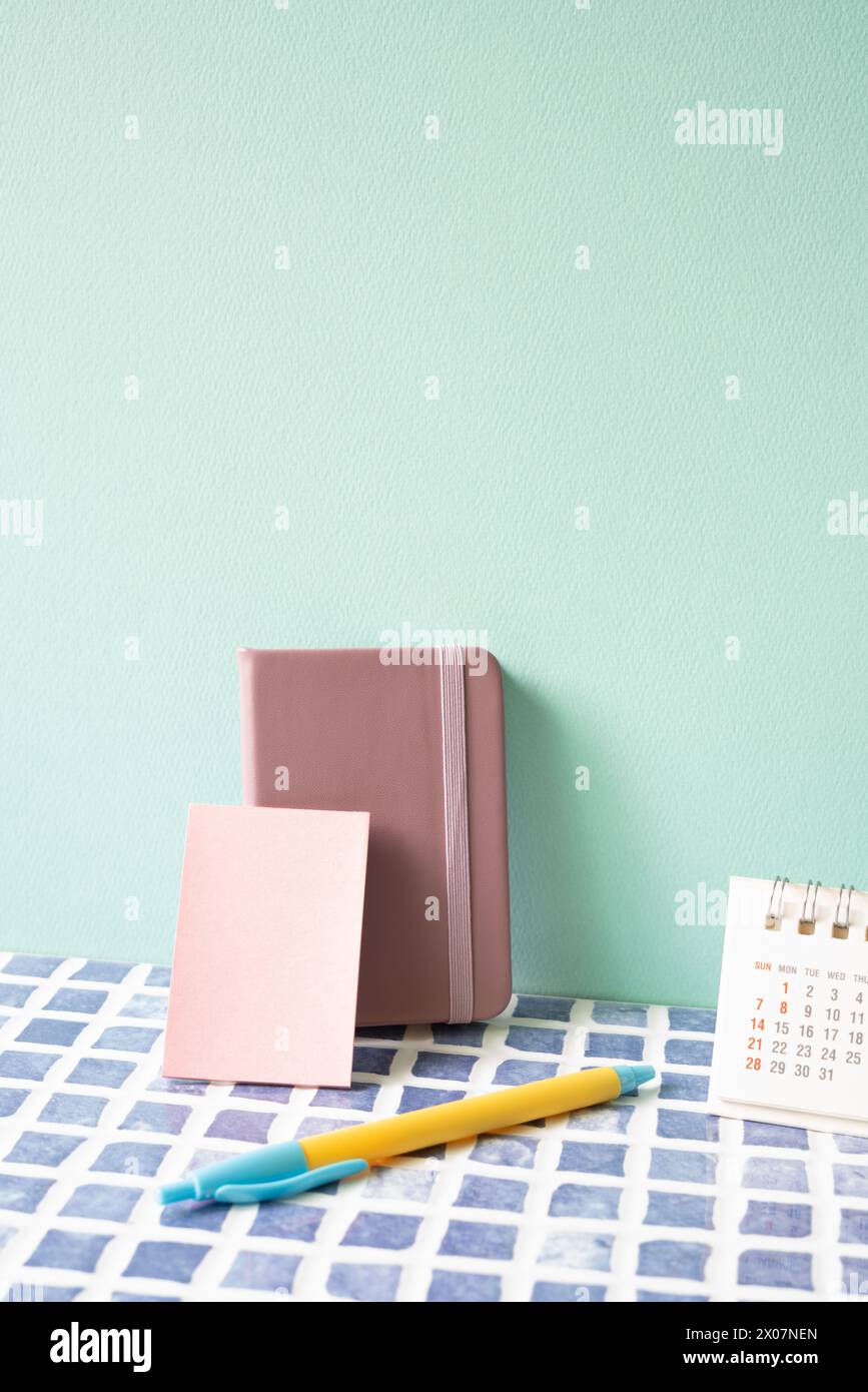 Diary note, pen, and calendar on blue tile desk. mint wall background ...