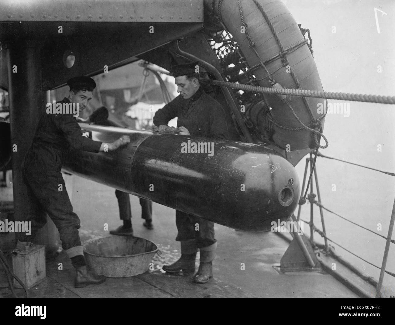 Torpedo men aboard HMS Kipling clean a torpedo protruding from its tube ...